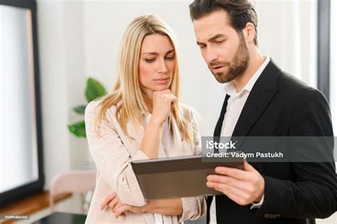 손에 디지털 태블릿을 가진 아름다운 여성과 진지한 남자가 사무실에 서서 태블릿 화면을 지켜보고 있습니다 20 24세에 대한 스톡 사진 및 기타 이미지 Istock