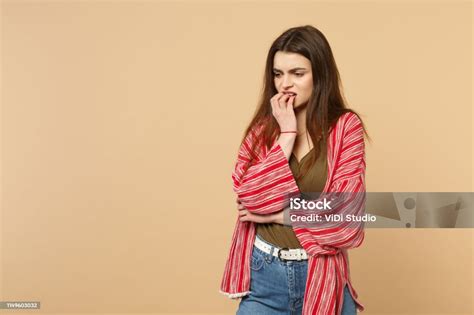 캐주얼 의류에 실망 젊은 여자의 초상화 스튜디오에서 파스텔 베이 지 벽 배경에 고립 된 손톱을 갉 아 먹는 사람들은 진심으로 감정 라이프 스타일 개념입니다 복사 공간을 모의