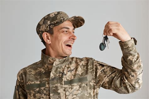 위장 유니폼과 모자를 쓰고 집 열쇠를 보여주고 재향 군인 단체의 모기지 지원을 보여주며 행복을 표현하는 행복한 흥분 군인의 실내 샷 퇴역군인에 대한 스톡 사진 및 기타