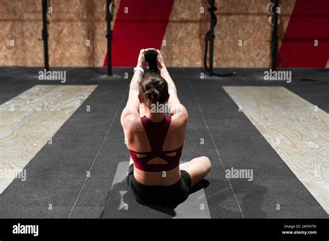 Back Of Sporty Caucasian Girl Sitting On Mat Doing Stretching Before