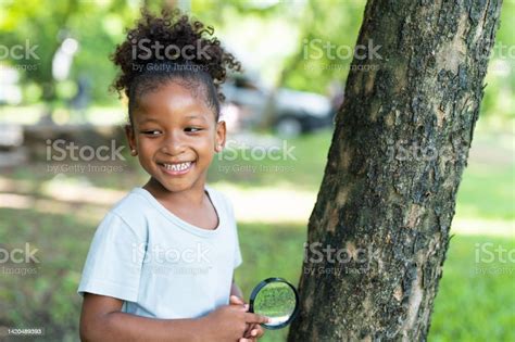 미소 짓는 아프리카 계 미국인 어린 소녀는 교실 밖에서 배우는 사이에 나무의 벌레를 탐험하고 볼 수있는 돋보기를 들고있는 재미를 느낍니다 교육 야외 개념 4 5세에 대한