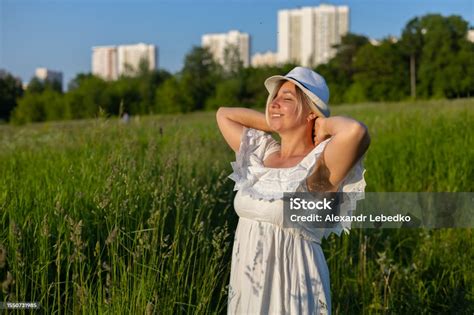 여름에 하얀 드레스를 입은 아름다운 여성이 머리카락 밑으로 손을 내밀어 눈을 감고 일몰을 즐긴다 초록색 들판의 높은 집 뒤의