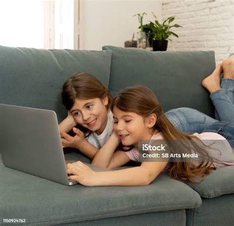 귀여운 어린 소녀와 누나가 함께 놀고 웃 고 집에서 소파에 노트북을 사용 하 여 시간을 본딩 행복 한 가족 형제 자매 관계와 디지털 기술 라이프 스타일 개념입니다 2명에