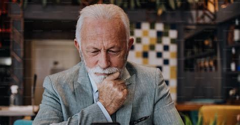 행복하고 잘 생긴 고위 사업가가 식당에 앉아 점심을 기다리고 있습니다 그는 스마트 폰을 사용하고 누군가와 이야기하고 있습니다 비즈니스 노인 라이프 스타일 개념입니다