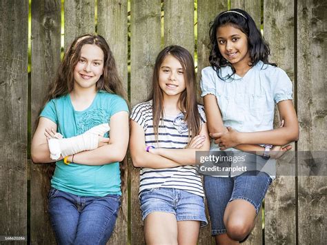 Three Smiling Preteen Girls Leaning Against A Fence High Res Stock