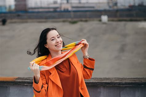 밝은 오렌지 망 토와 수조의 밝은 스카프에 검은 곱슬 머리와 함께 화려한 여자의 초상화 밝은 소녀 회색 항구에 걷는 아름 다운 여성의 눈의 행복 한 시선입니다 여자 재미