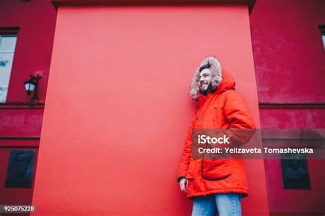 젊은 잘생긴 남자 빨간색 겨울 자 켓에 수염과 학생 및 교육 기관의 건물의 붉은 벽의 배경에 모피와 후드의 초상화 12월에 대한 스톡 사진 및 기타 이미지 Istock