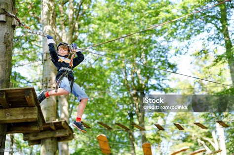 숲 모험 공원에서 학교 소년 헬멧을 쓰고 있는 아이는 높은 로프 트레일에서 올라간다 민첩성 기술과 어린이를위한 야외 놀이 센터를 등반 어린이 및 가족을위한 야외 활동 고등