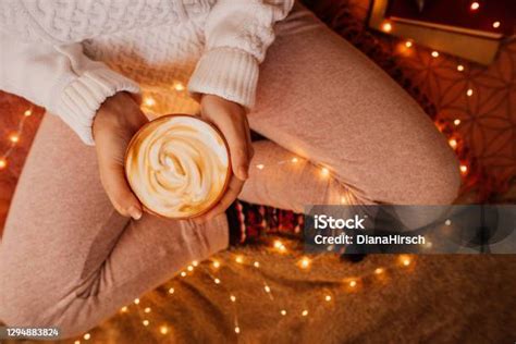 그녀의 손에 그녀의 크림 아침 커피를 들고 아늑한 가정 의류에 작은 조명을 가진 인식 할 수없는 젊은 여자 양모에 대한 스톡 사진 및 기타 이미지 Istock