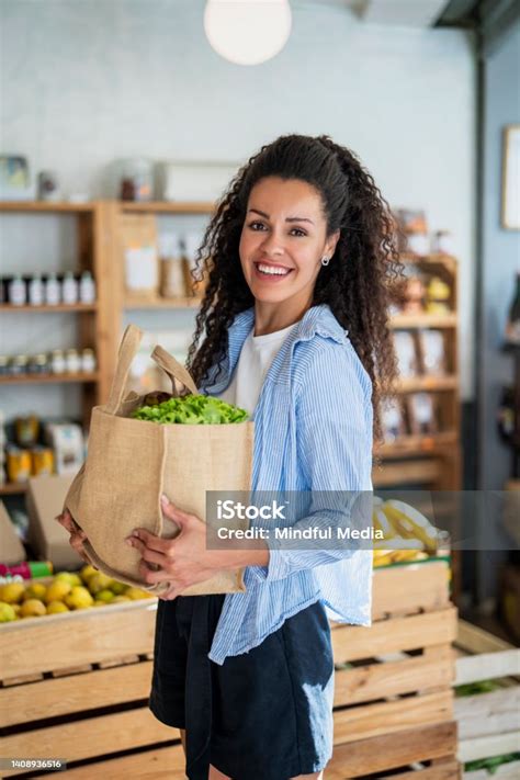 그녀의 유기농 식료품 점 안에 가방을 들고 다니는 젊은 여성 아프리카 계 미국인 중소기업 주인의 중간 샷 뷰 식료품상에 대한 스톡 사진 및 기타 이미지 Istock