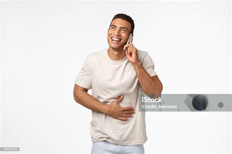 남자는 전화로 이야기 재미있는 농담을 들었다 척에서 배가 아파요 잘생긴 젊은 남자는 귀 근처에 스마트 폰을 잡고 고개를 들고 평온한 미소를 지으며 큰 소리로 웃고 흰색