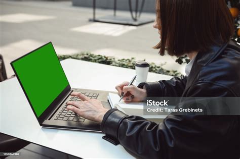 여성 프리랜서 카피라이터 메모장에 텍스트를 쓰고 모니터에 녹색 화면 크로마 키가 있는 랩톱 컴퓨터의 키보드를 입력하는 측면 초상화 온라인 원격 작업 및 프리랜서 개념