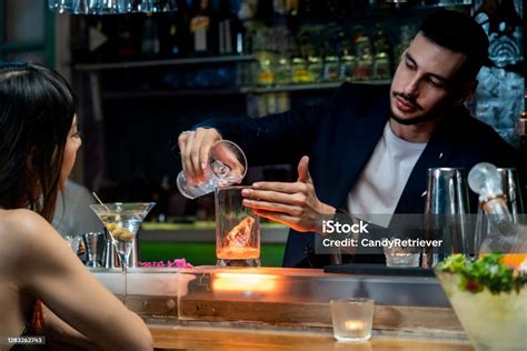 전문 남성 믹솔로지스트 바텐더가 나이트클럽의 바 카운터에 앉아 있는 여성에게 서빙하는 혼합 알코올 칵테일 음료를 준비하고