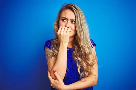 젊은 아름다운 여자는 파란색 고립 된 배경 위에 서 스트레스와 손톱을 물고 입에 손으로 긴장 찾고 불안 문제 T 셔츠에 대한