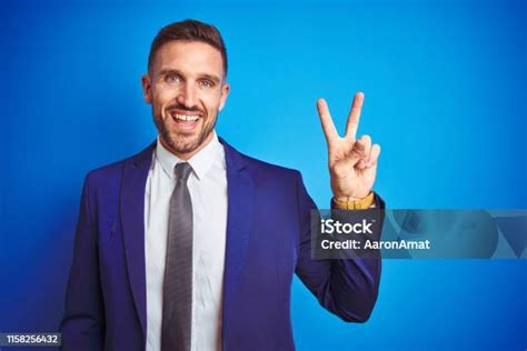 파란색 고립 된 배경을 통해 젊은 잘 생긴 사업가 는 승리 기호를하고 카메라에 윙크 행복한 얼굴미소 2번 경영자에 대한 스톡 사진 및 기타 이미지 Istock