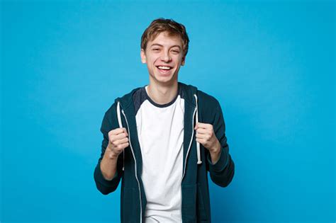 매력적인 웃는 즐거운 젊은 남자의 초상화는 스튜디오에서 파란색 벽 배경에 고립 된 주먹을 쥔 서 있는 복장 사람들은 진심으로 감정 라이프 스타일 개념입니다 복사 공간을 모의