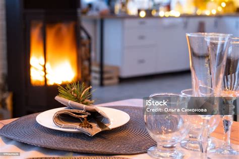 크리스마스와 새해를 위해 장식 된 로프트 하우스 내부의 스토브 벽난로 근처에서 접시 포크 나이프 냅킨 안경이있는 축제 테이블을