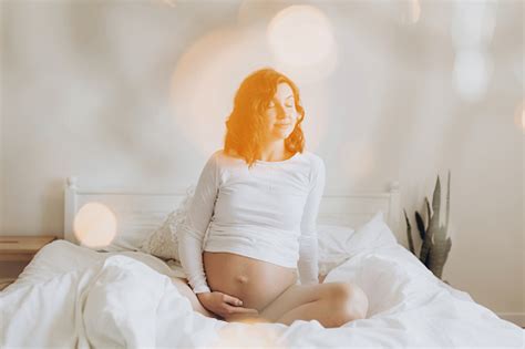 아기를 기다리고 사랑과 배려와 함께 배를 포옹 하는 세련 된 임신한 엄마 어머니의 개념 마법의 시간 행복 한 임신한 여자에 흰색을 들고 배꼽 범프와 휴식에 흰색 침대에서 집