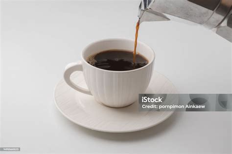 테이블 위의 하얀 컵에 커피를 붓는 모카포트를 들고 있다 흰색 배경에 분리된 흰색 컵에 담긴 블랙 커피 브루드 커피에 대한 스톡