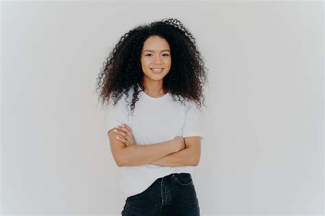 아프로 헤어 스타일과 평온한 젊은 아름다운 여자의 스튜디오 샷 팔을 접고 즐겁게 미소 흰색 배경에 고립 캐주얼 티셔츠와 청바지를 입고 사람 민족 얼굴 표정 T 셔츠에 대한