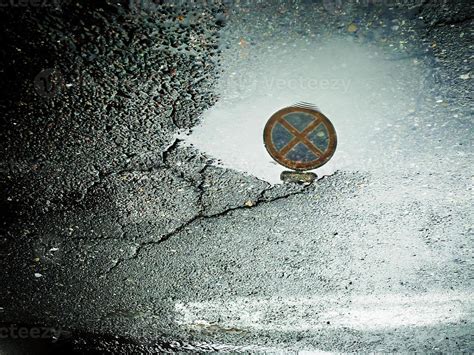 Road Sign Reflected On Water Surface Wet Cracked Asphalt Background