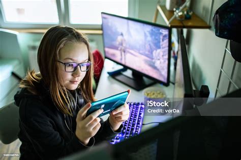 데스크톱 컴퓨터 옆 침실에서 스마트폰으로 게임을 하는 어린 소녀 12 13세에 대한 스톡 사진 및 기타 이미지 12 13세 Brand Name Video Game E