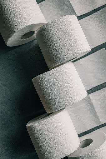 어두운 배경에 흰색 화장지 롤이 대각선으로 배열된 미니멀한 구성으로 일부는 부분적으로 펼쳐져 부드러운 자연광에서 질감과 패턴을 보여줍니다 위생에 대한 스톡 사진 및 기타