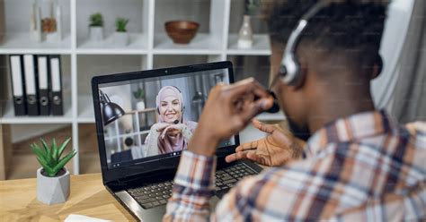 아프리카계 미국인 남자와 무슬림 여자가 집에 있는 동안 화상 통화 중에 이야기하는 뒷모습 헤드셋과 현대적인 노트북을 사용하여 먼 거리에서 의사 소통하는 사랑스러운 커플