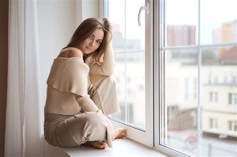 창틀에 앉아 향기로운 커피 한 잔을 들고 있는 동안 바쁜 도시의 창 밖으로 바라보는 사려 깊고 꿈꾸는 소녀 가을에 대한 스톡 사진 및 기타 이미지 Istock