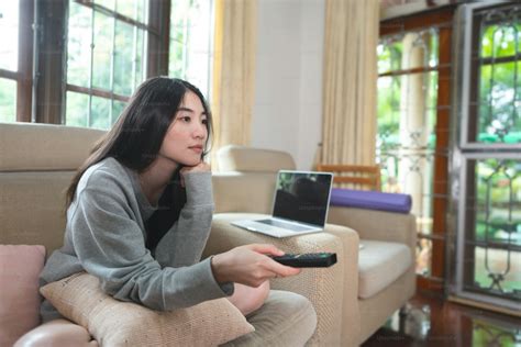 젊은 성인 아시아 여성은 거실에서 집에서 하루에 인터넷을 통해 온라인 영화를 보기 위해 원격 tv를 사용합니다 소파에 앉아