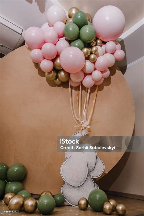 아치는 분홍색 황금색 녹색 풍선 종이 장식 코끼리 색종이로 장식되어 있습니다 갈색 사진 벽에 소녀 또는 소년을 위한 생일 파티 어린이 포토존 축하 세례 개념입니다 텍스트를