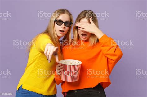두 깜짝 놀란 젊은 금발의 쌍둥이 자매 여자 3d 아이맥스 안경을 보고 영화 필름을 들고 팝콘에 고립 된 파스텔 바이올렛 블루 벽 배경 사람들 가족 라이프 스타일 개념입니다