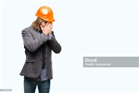 우는 동안 손으로 얼굴을 덮고 슬픈 표정으로 격리 된 배경 위에 안전 헬멧을 쓰고 긴 머리를 가진 젊은 잘생긴 Architec