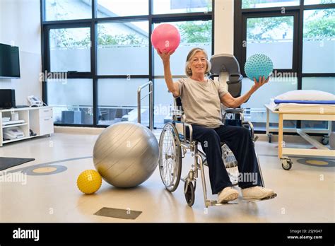 A Cheerful Senior Woman Sitting In A Wheelchair Engages In Physical