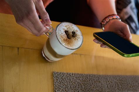 아침 카푸치노의 흰색 컵을 들고 흰색 세련된 드레스를 입고 빈티지 하트 선글라스를 테이블에 올려 놓고 혼자 시간을 보내는 여성의 패션 이미지를 닫습니다 인스 타 그램 색상