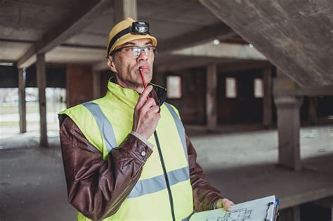 건설 현장에서 설계자 독서 계획의 초상화 안전 조끼를 입은 안전 헬멧을 착용한 토목 엔지니어가 디지털 태블릿을 사용합니다 적응