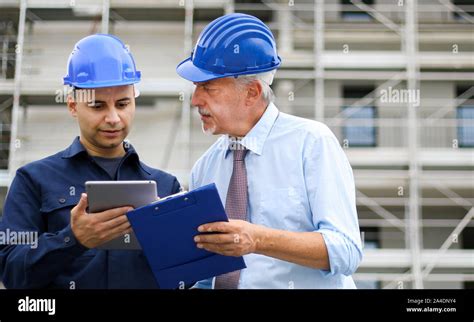 Two Architect Developers Reviewing Building Plans At Construction Site