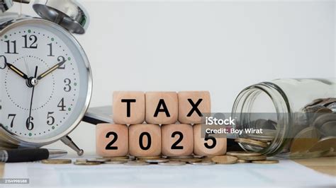 세금 및 부가가치세 2025 개념 이 이미지는 알람 시계 동전 병 펜 및 나무 블록으로 Tax 2025를 철자합니다 납부를 위한 소득세 온라인 신고서 비용 계정 Vat 세금