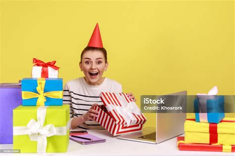 직장에 앉아 선물 상자를 열고 놀란 즐거운 표정으로 카메라를 바라 보는 여성 25 29세에 대한 스톡 사진 및 기타 이미지 25 29세 경외감 공휴일 Istock
