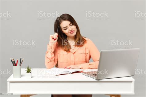 메모를 쓰고 앉아서 회색 배경에 고립 된 Pc 노트북으로 흰색 책상에서 일 하는 젊은 파스텔 캐주얼에서 여자 의아해 성취