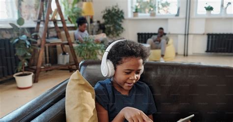 헤드폰을 끼고 검은 가죽 소파에 베개로 앉아 부모에 대해 디지털 태블릿 화면을 가리키는 사랑스러운 어린 소년 사진 Unsplash의 어린이 전용 이미지