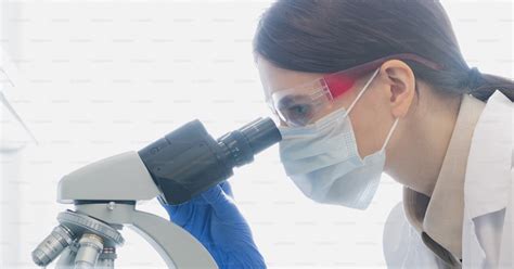 현대 실험실에서 현미경을 사용하여 표본 화학 반응을 조사하는 알아볼 수 없는 여성 의료 과학자의 수직 측면도 샷 사진