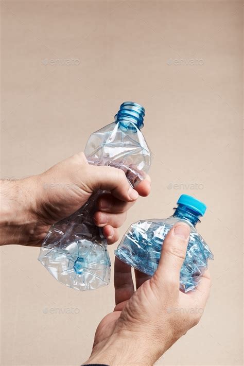 Male Hand Holding Squashed Plastic Bottle Over Paper Background Stock