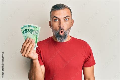 Middle Age Handsome Man Holding 10000 South Korean Won Banknotes Scared And Amazed With Open