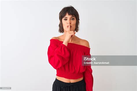 빨간 여름 티셔츠를 입은 젊은 아름다운 여성은 입술에 손가락으로 조용히 달라고 요청하는 고립 된 흰색 배경 위에 서 있습니다 침묵과 비밀 개념 T 셔츠에 대한 스톡 사진 및