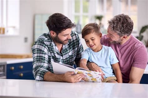 Same Sex Family With Two Dads And Son Reading Book In Kitchen At Home