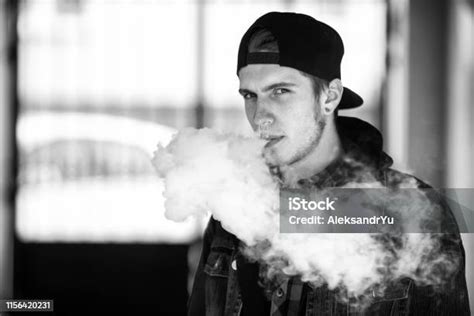 Vape 십대 여름에 거리에서 전자 담배를 피우는 모자에 젊은 잘 생긴 남자의 초상화 나쁜 습관 20 24세에 대한 스톡 사진 및 기타 이미지 Istock