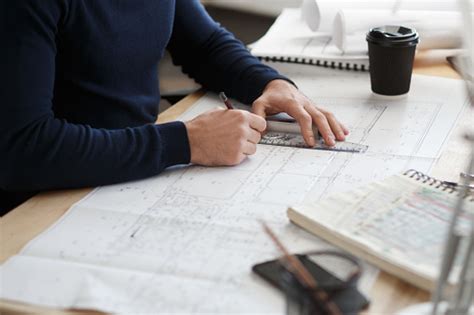 청사진이 있는 사무실에서 일하는 건축가 엔지니어가 건설 프로젝트를 스케치하여 건축 계획을 검사합니다 직장에 앉아 잘 생긴 수염 남자의 초상화 비즈니스 건설 개념 갈색 머리에