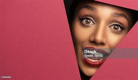 밝은 메이크업과 통통한 빨간 입술을 가진 젊은 아름다운 소녀의 얼굴이 분홍색 종이의 구멍을 들여다 보입니다 25 29세에 대한 스톡 사진 및 기타 이미지 Istock