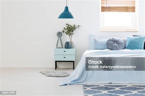 밝은 파란색 침대와 빈 벽 사이 나무 스탠드와 파란과 백색 침실 인테리어의 실제 사진 안락의 자 여기 붙여넣기 0명에 대한 스톡